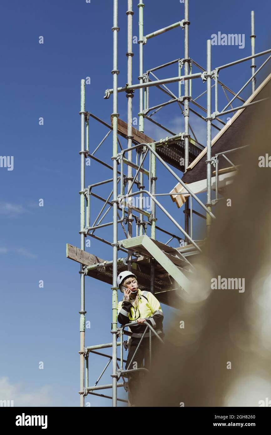 Female builder talking on mobile phone while standing at scaffolding ...