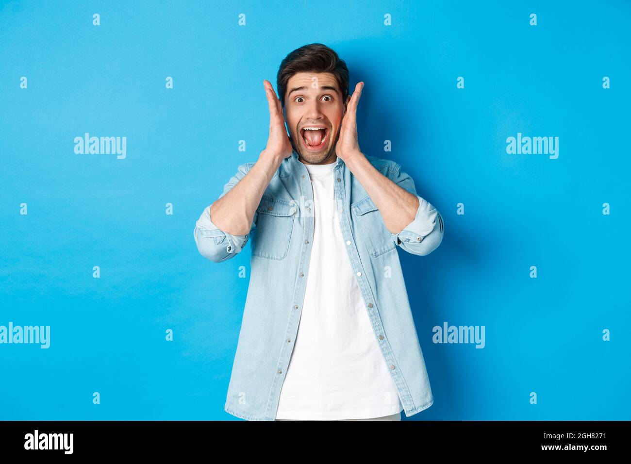 Scared man screaming and looking startled at something, standing against blue background Stock ...