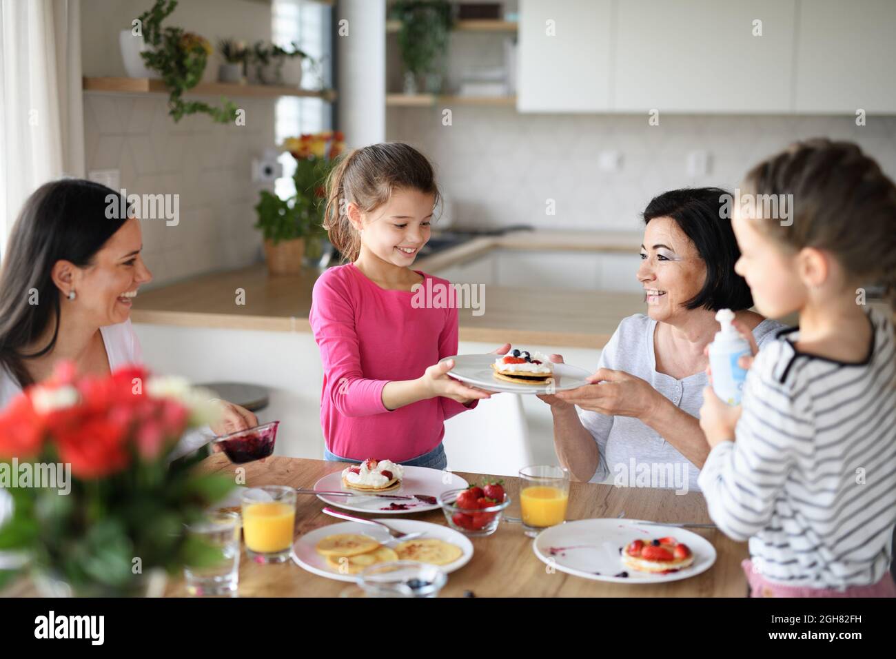 Happy small girls with mother and grandmother eating pancakes indoors ...