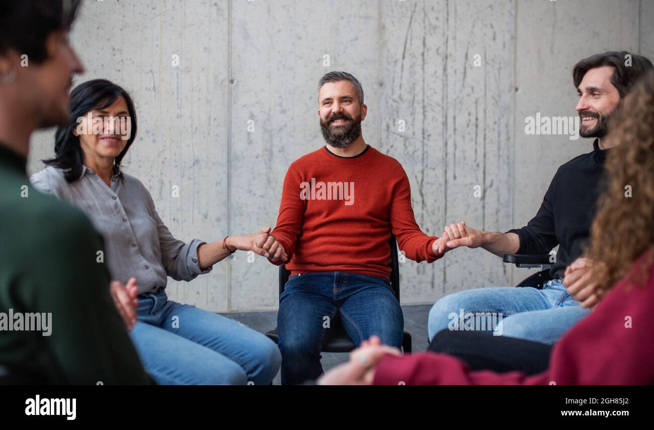 Men and women sitting in circle during group therapy, holding hands ...