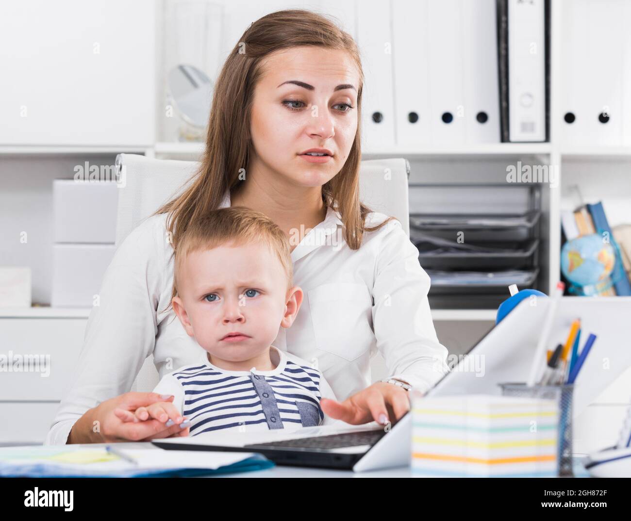 Perplexed female with child is having problems while working in office ...