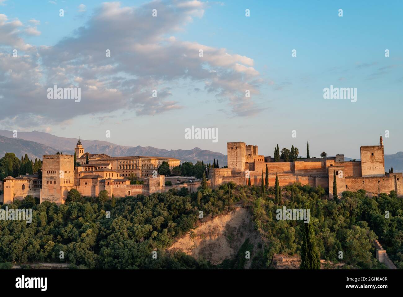Horizontal view of Alhambra Palace and green trees under blue cloudy ...