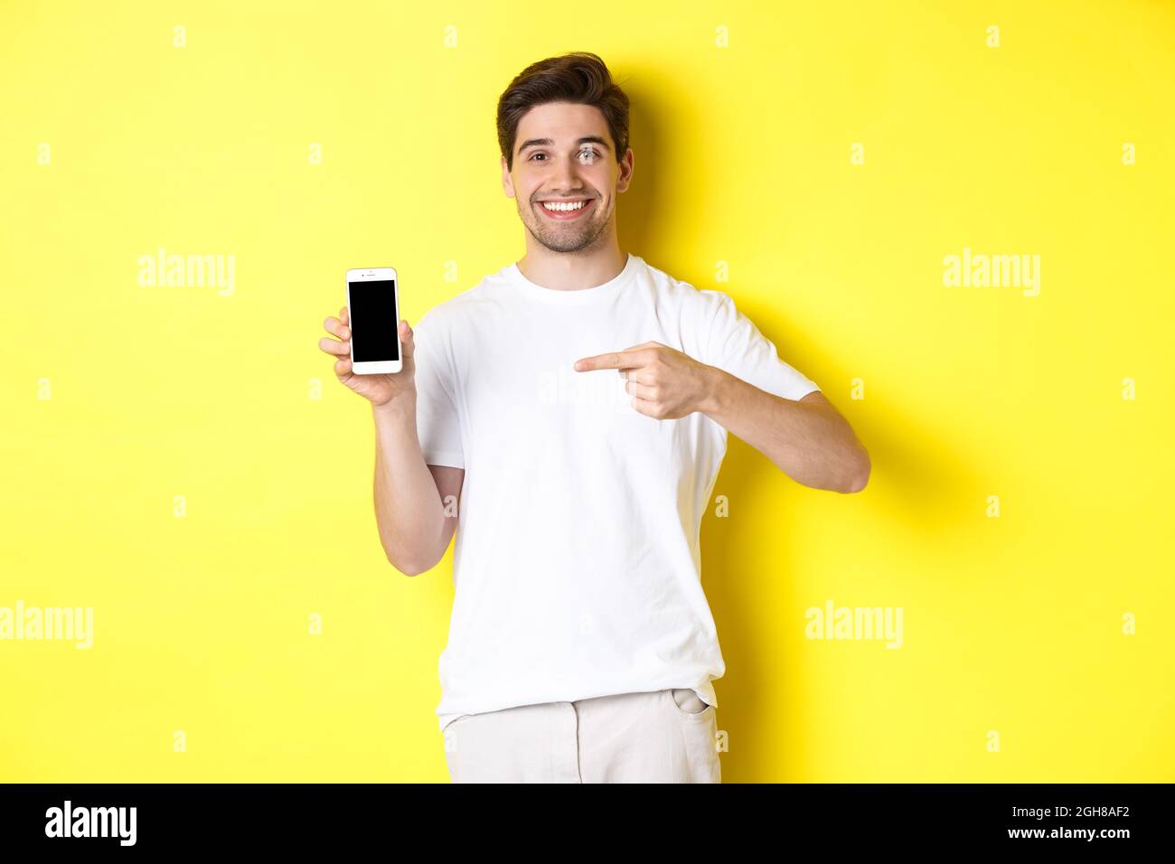 Image of attractive young man pointing finger at smartphone screen ...