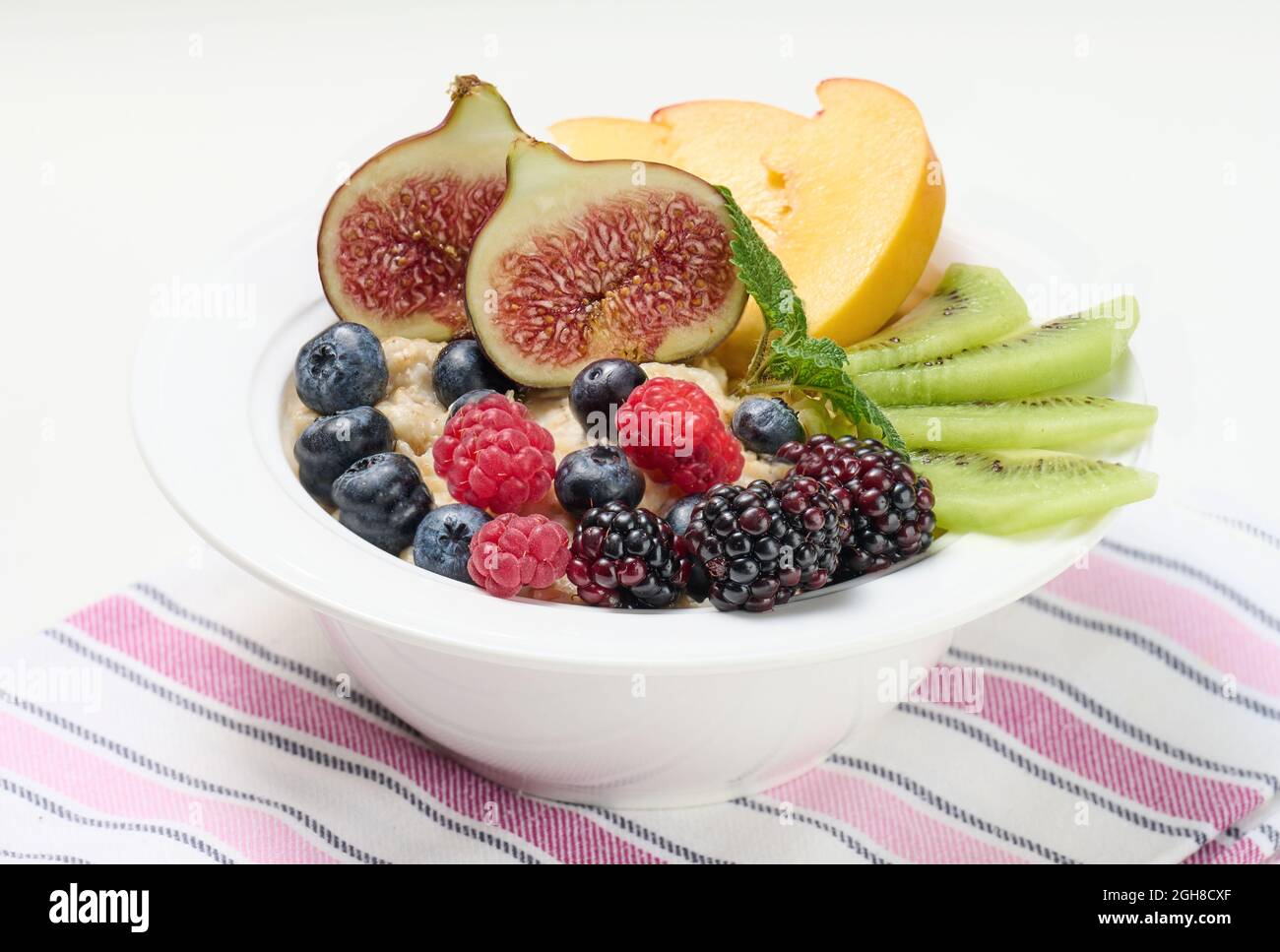boiled oatmeal porridge with fruit in a round plate on a white table ...