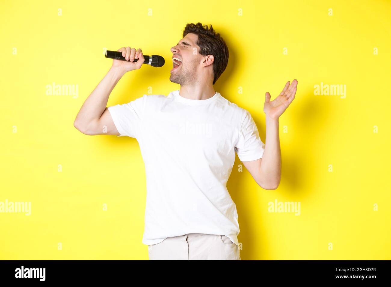Young man singer holding microphone, reaching high note and singing ...