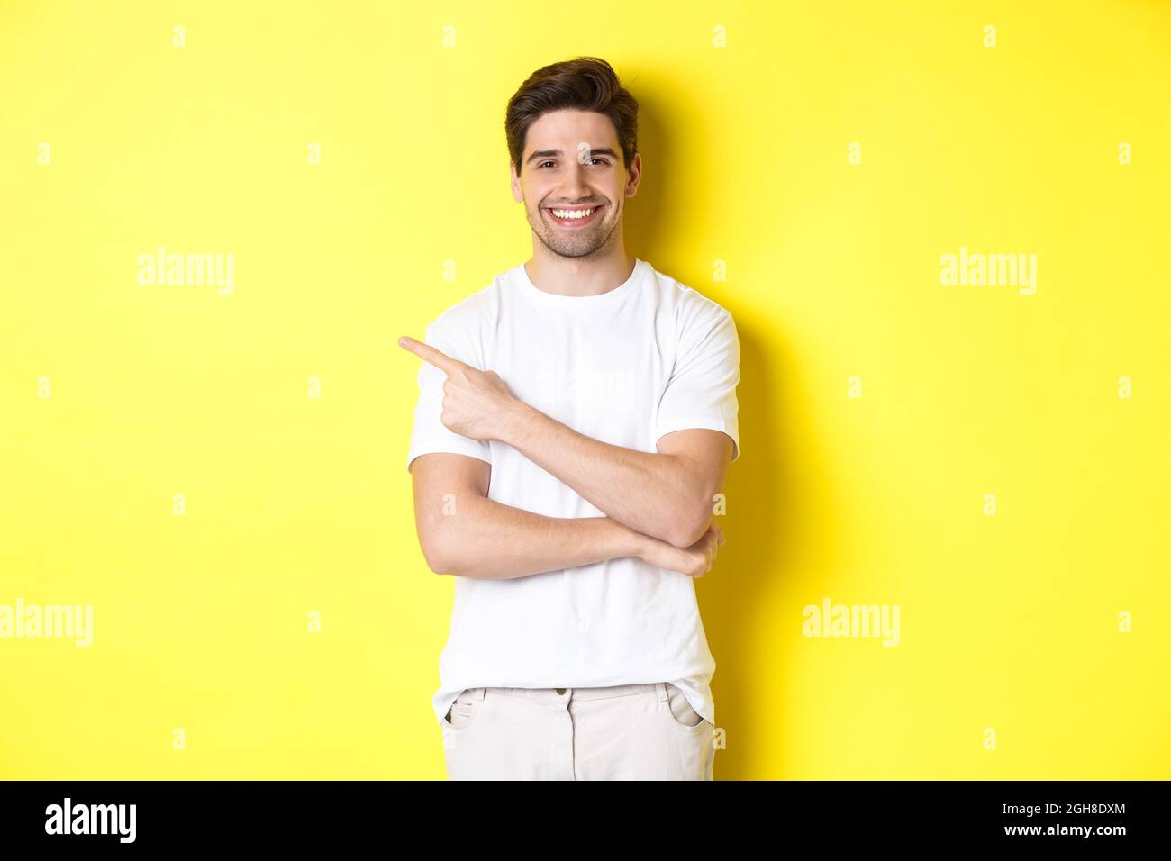 Handsome guy pointing left and smiling, showing advertisement on yellow ...