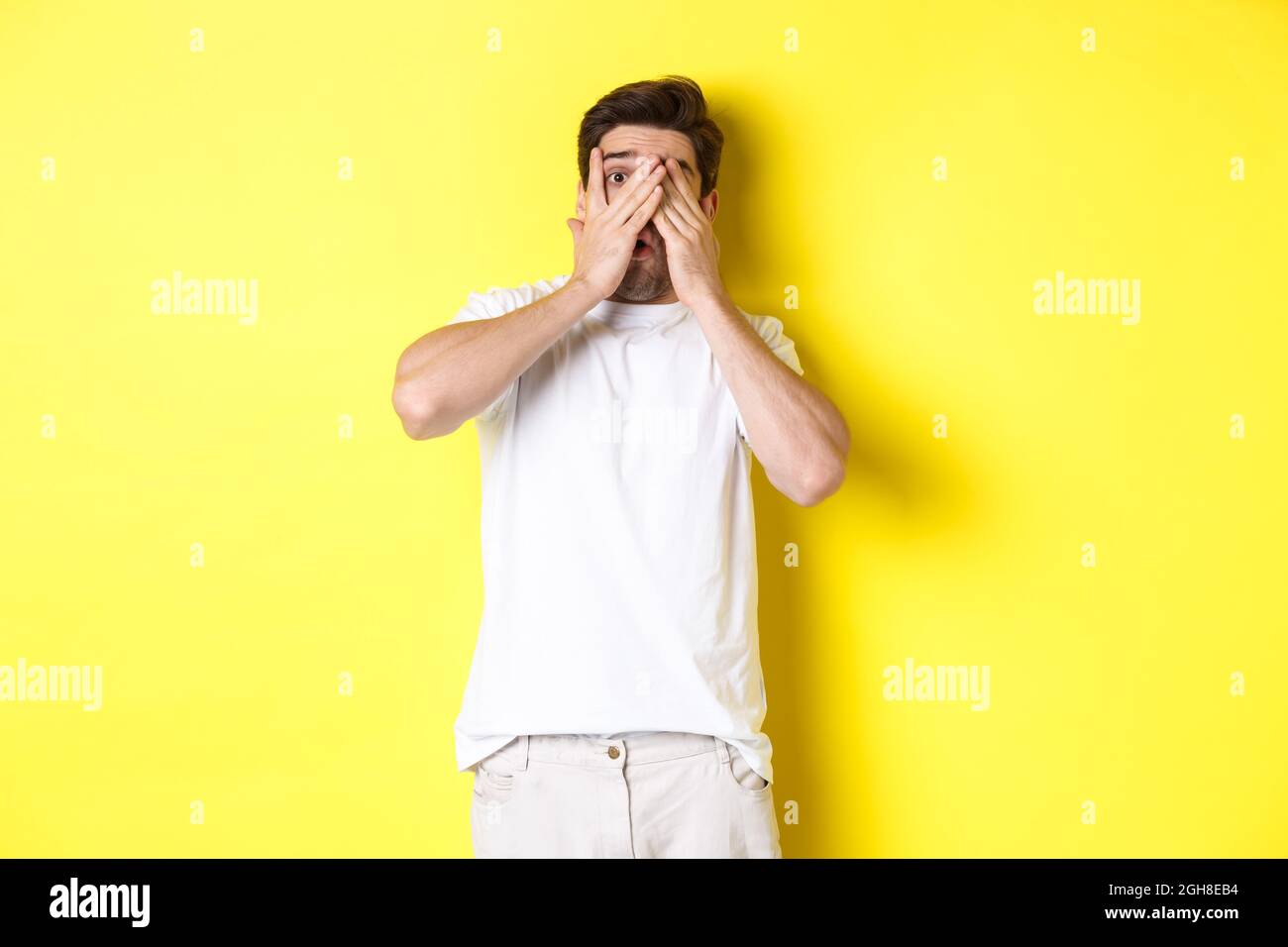 Embarrassed guy shut eyes but peeking through fingers at something ...