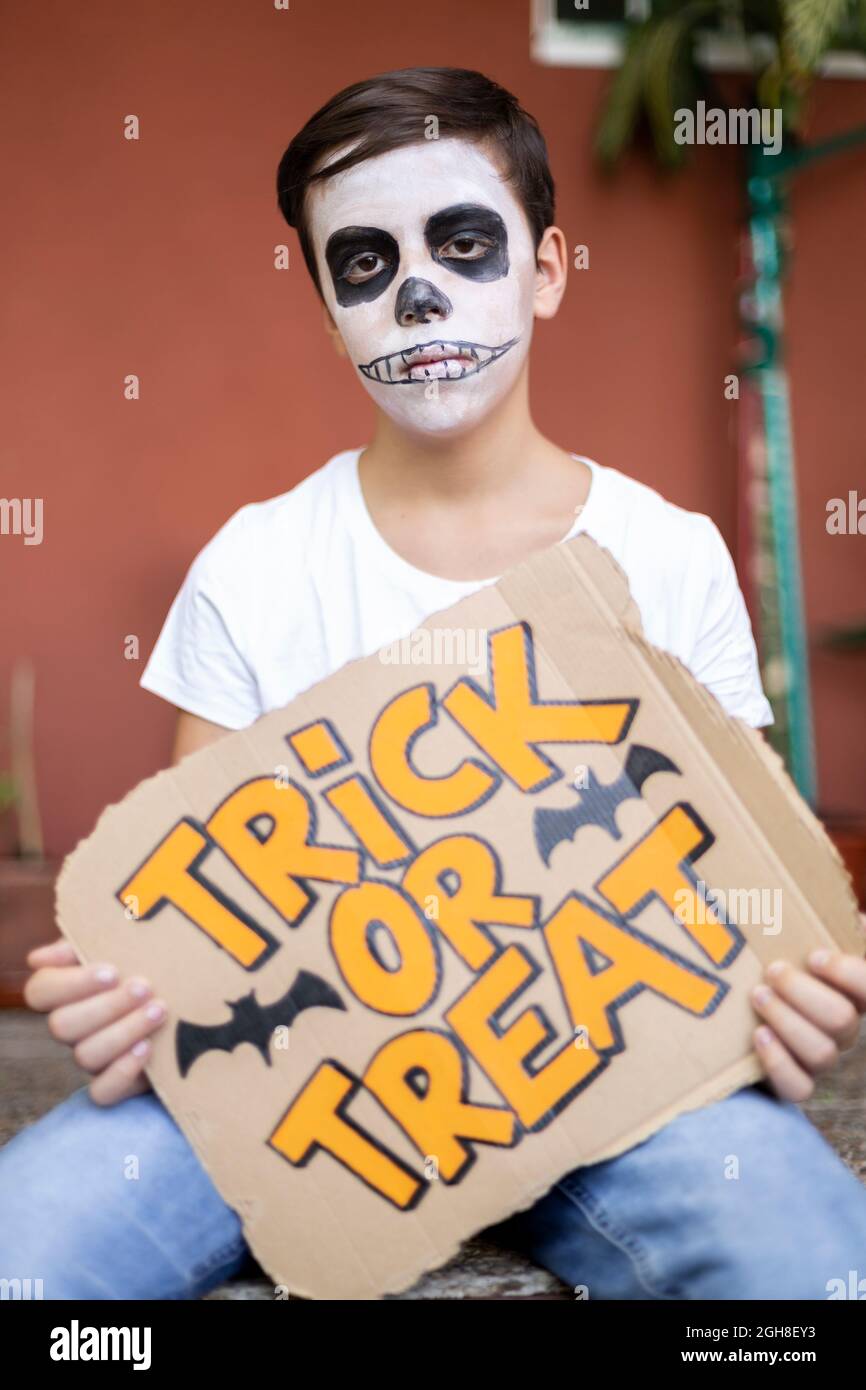 Portrait of boy with face characterized as a skull sitting outdoors. He ...