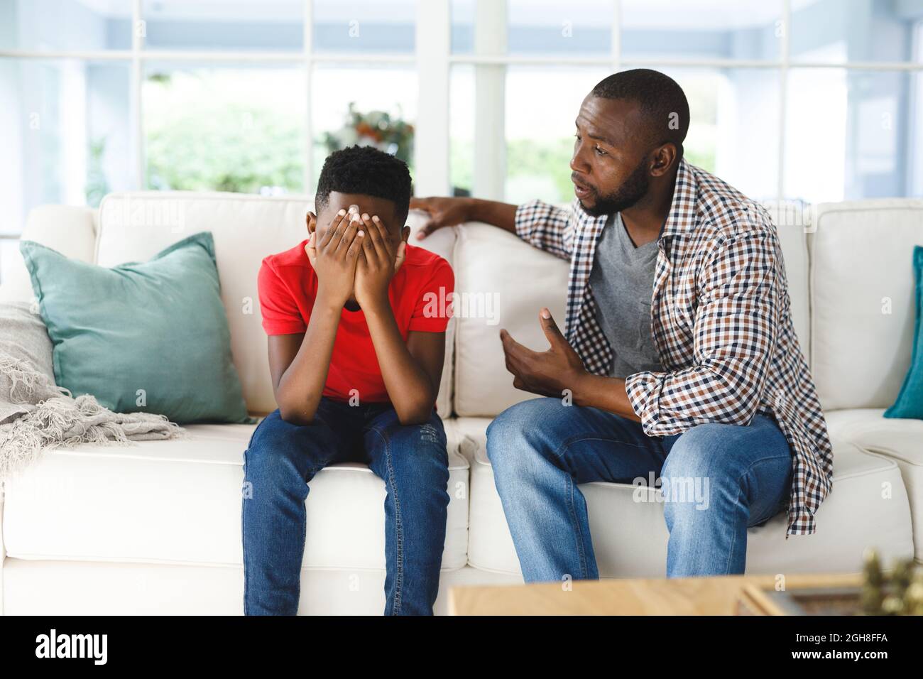 Sad african american son sitting on couch covering face listening to ...