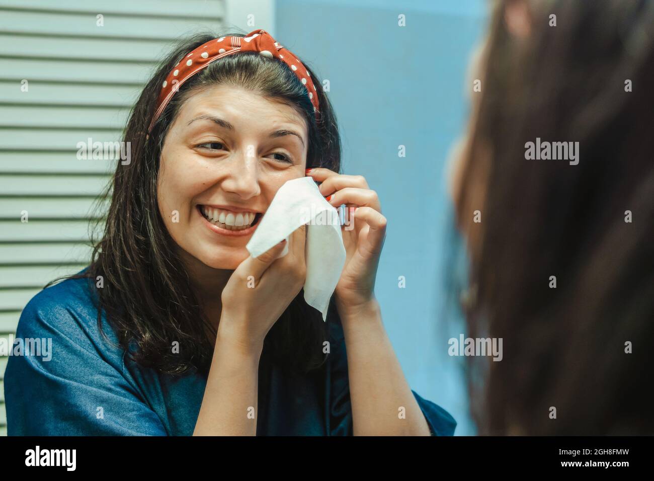 Young happy woman makes a facial treatment smiling in the mirror ...