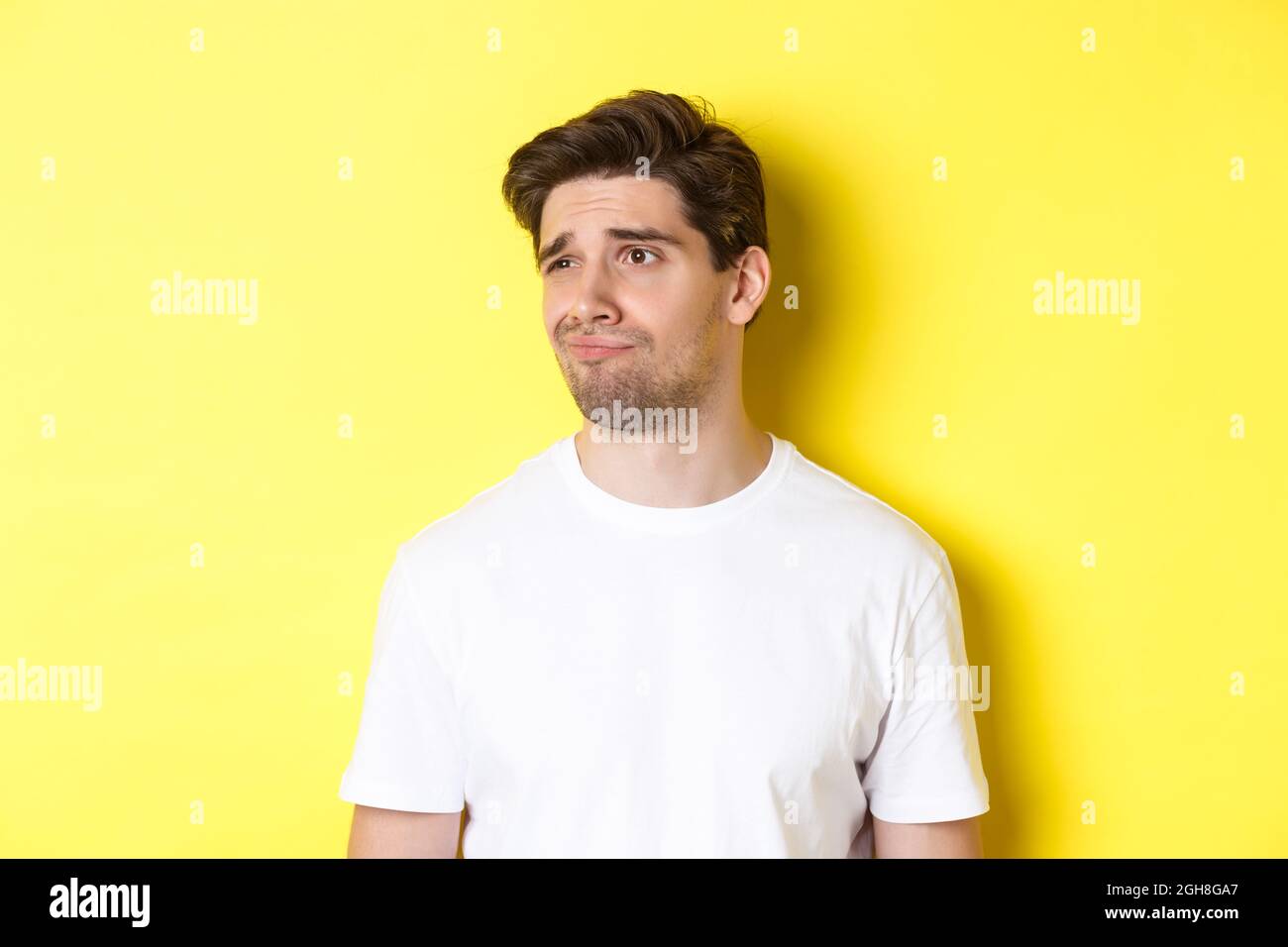 Reluctant guy in white t-shirt looking left, grimacing skeptical and ...