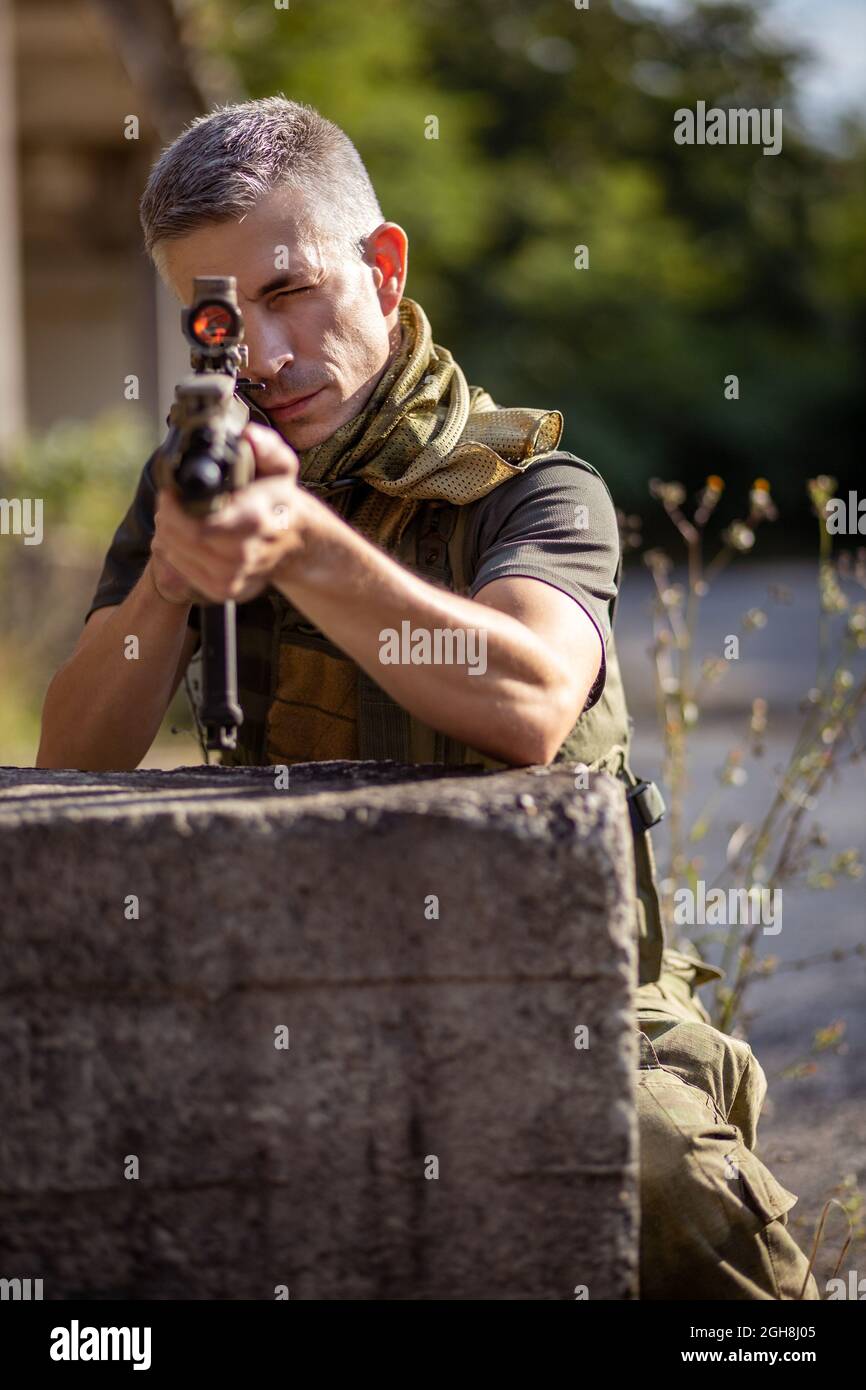 A man kneels behind the cover with an airsoft assault rifle in military ...