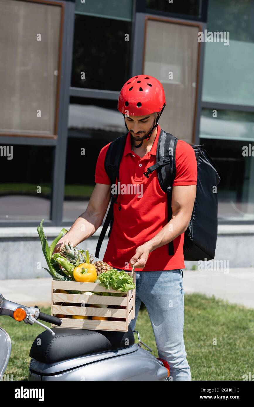 Young arabian courier in safety helmet holding wooden box with ...