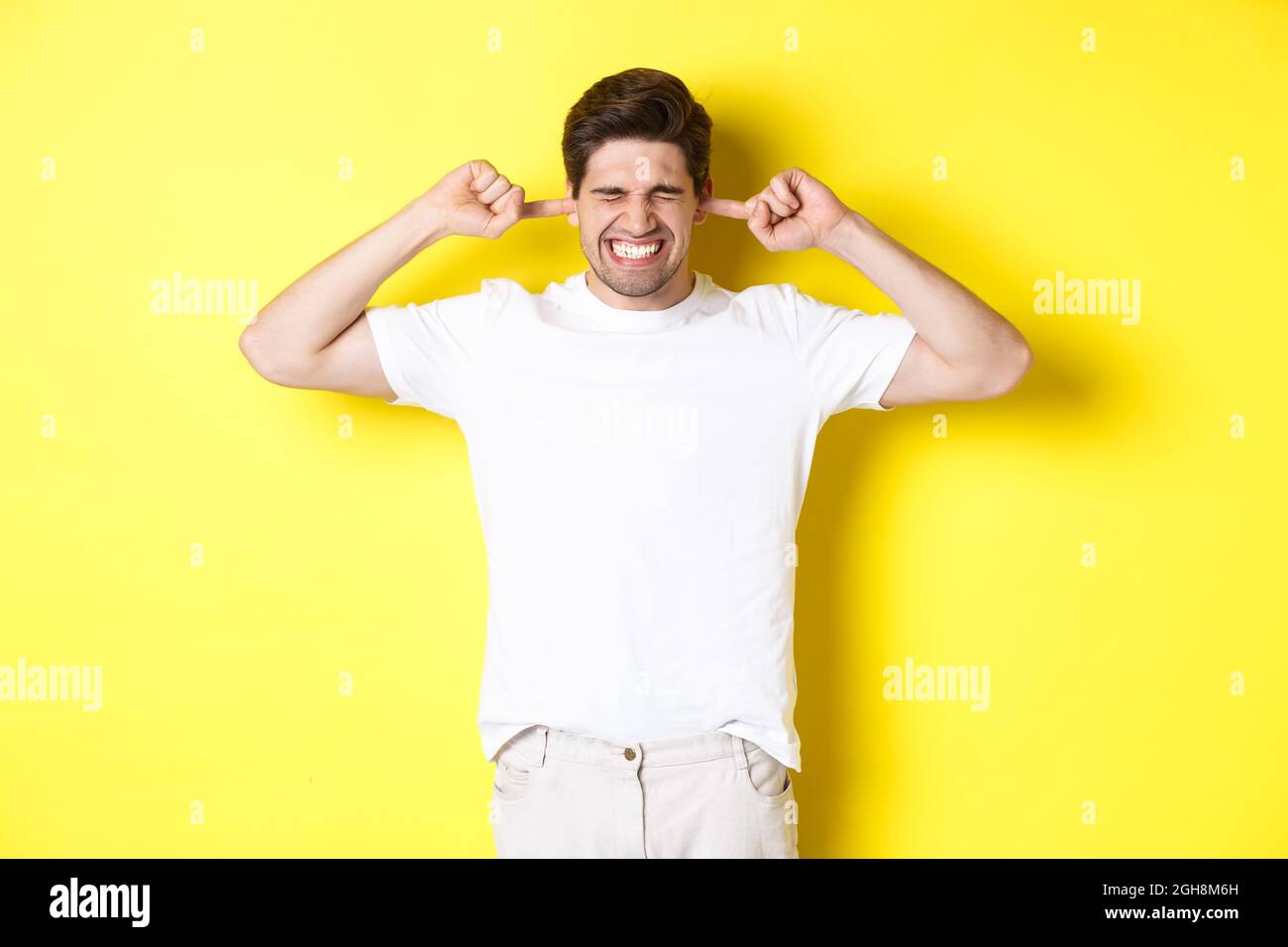 Annoyed man grimacing and shutting ears, complaining on loud noise ...