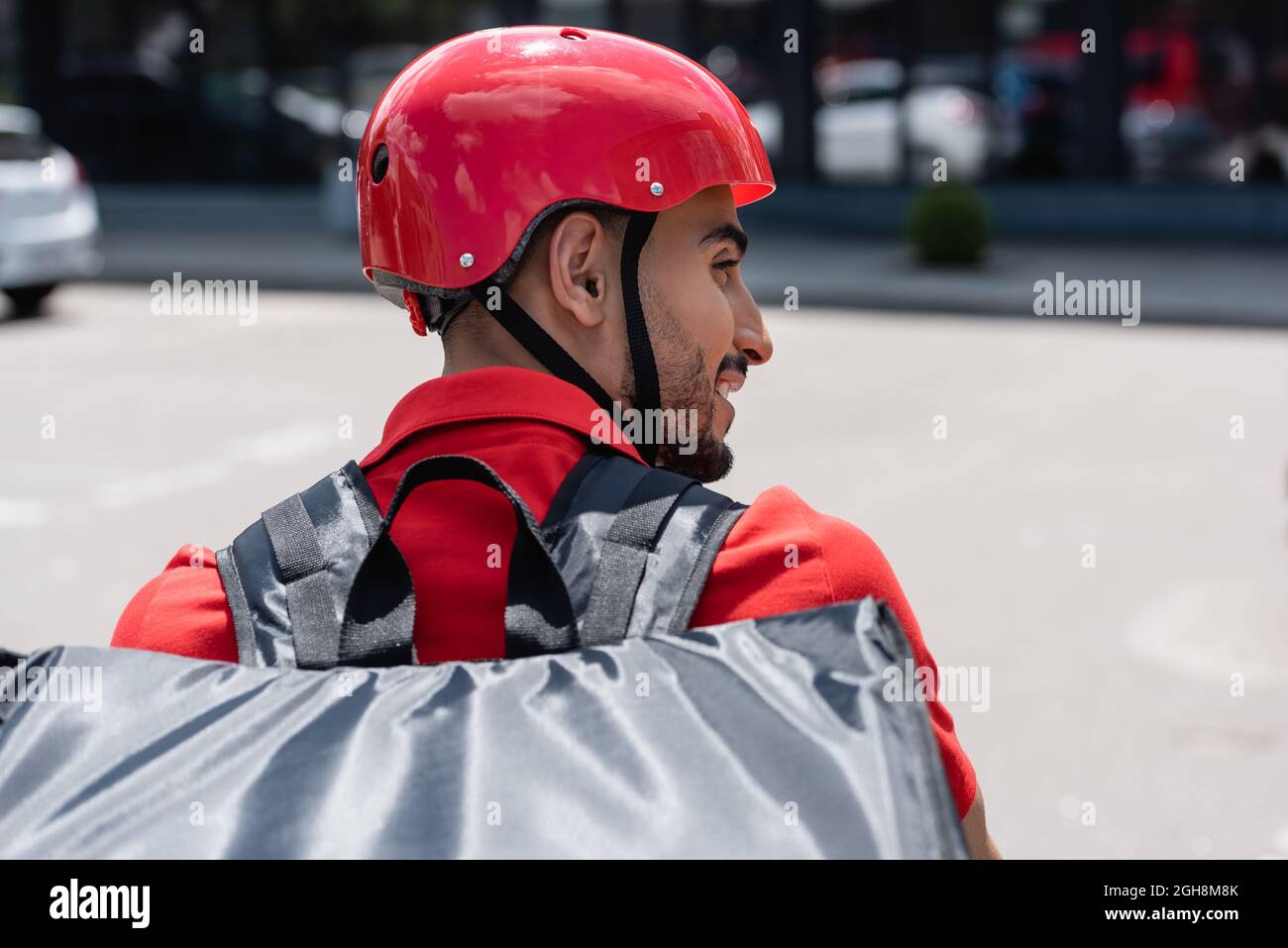 Side view of muslim deliveryman in helmet and thermo backpack outdoors ...