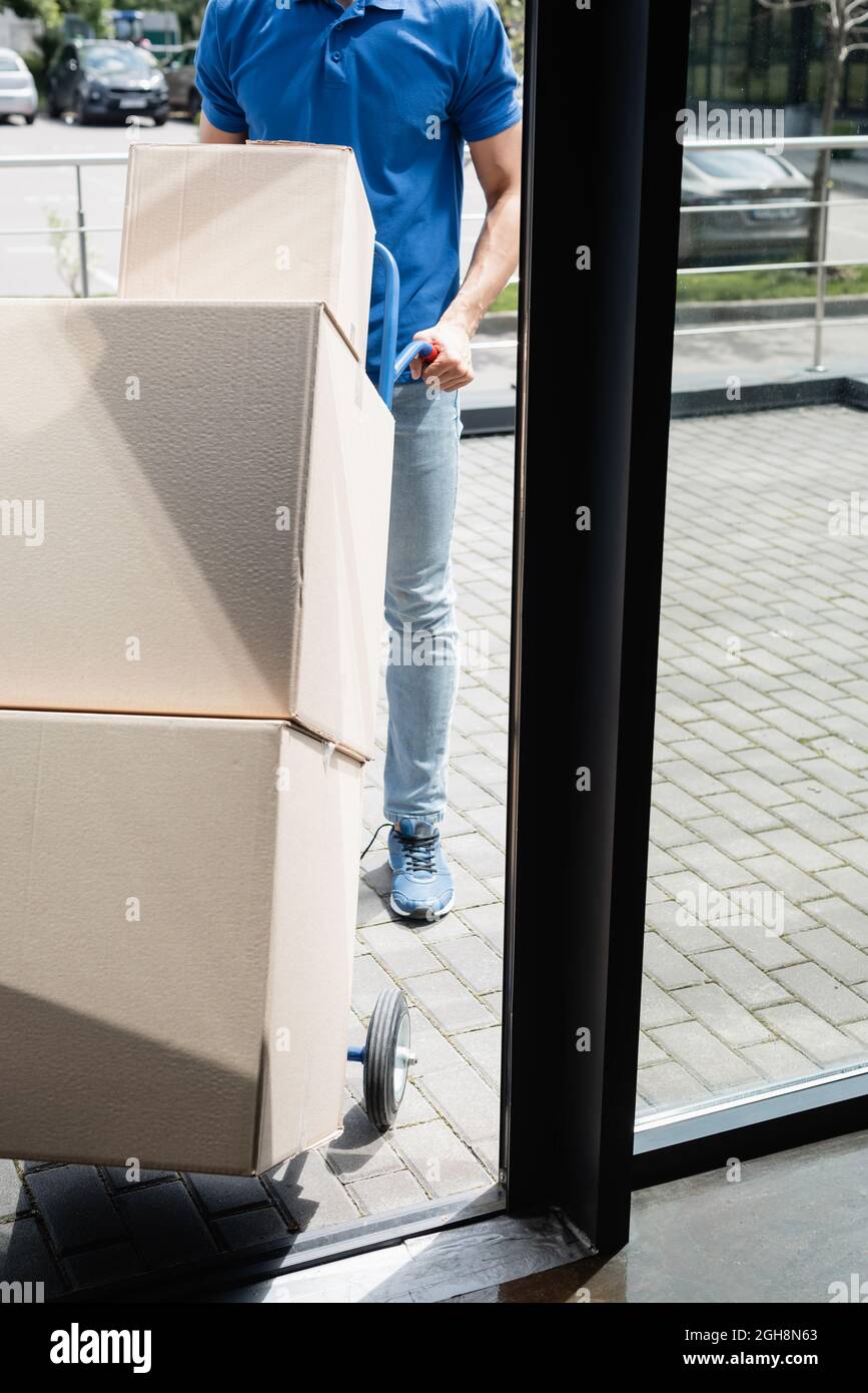 Cropped view of courier holding cart with carton boxes near door Stock ...