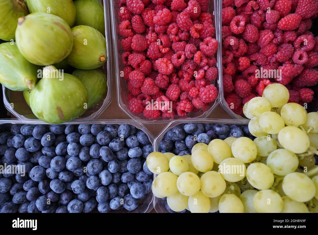 Top view shot of grapes, red raspberries, blueberries, and figs in a ...