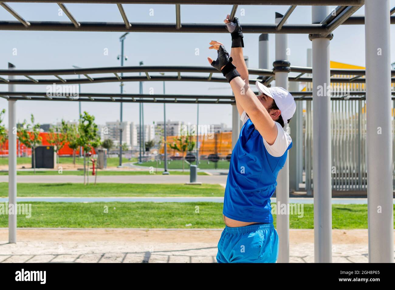 Side view of a young man hanging from the bars at the calisthenics gym ...