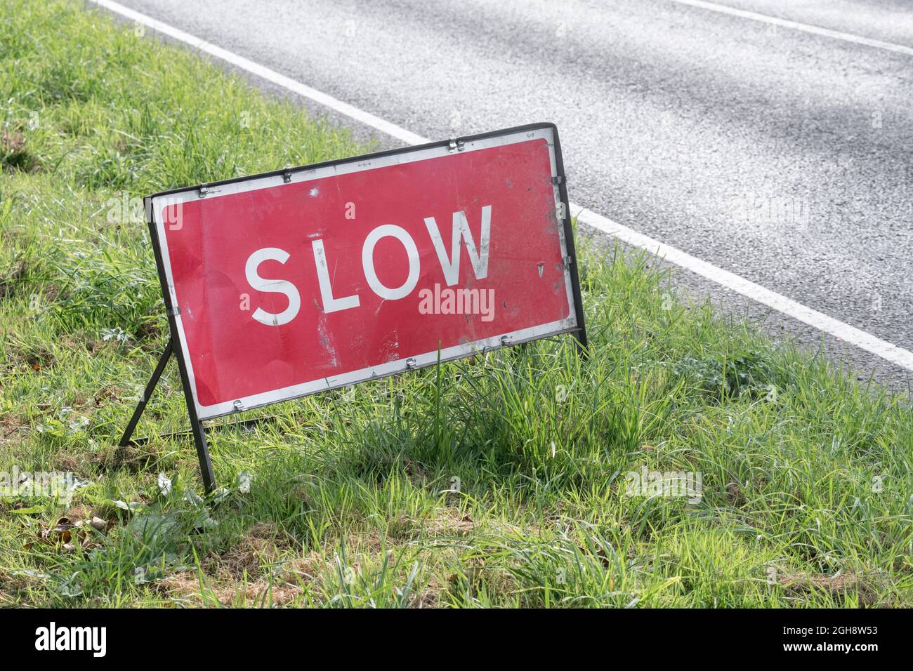 Red SLOW road sign on rural grass verge, warning of roadworks ...
