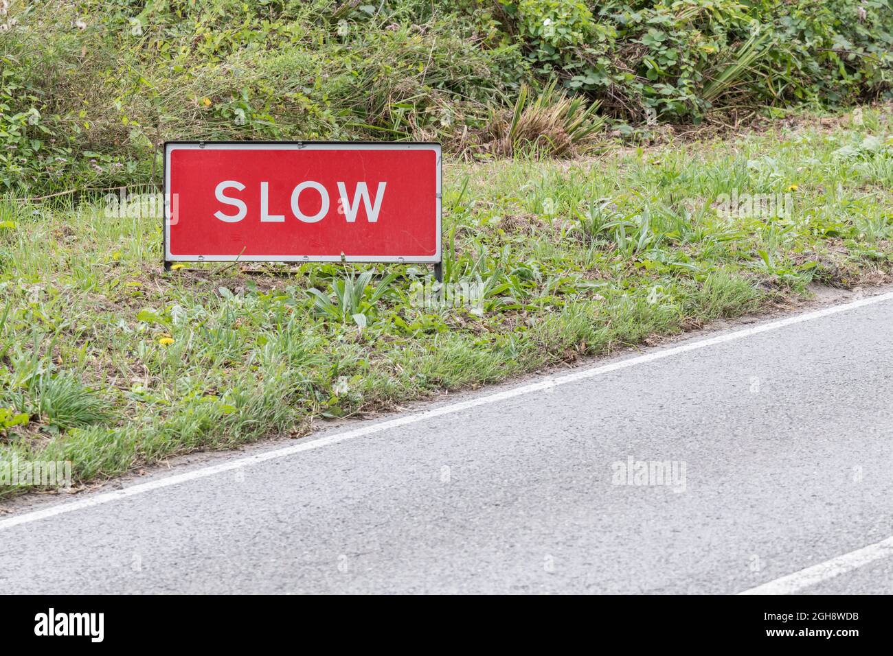 Red SLOW road sign on rural grass verge, warning of roadworks ...