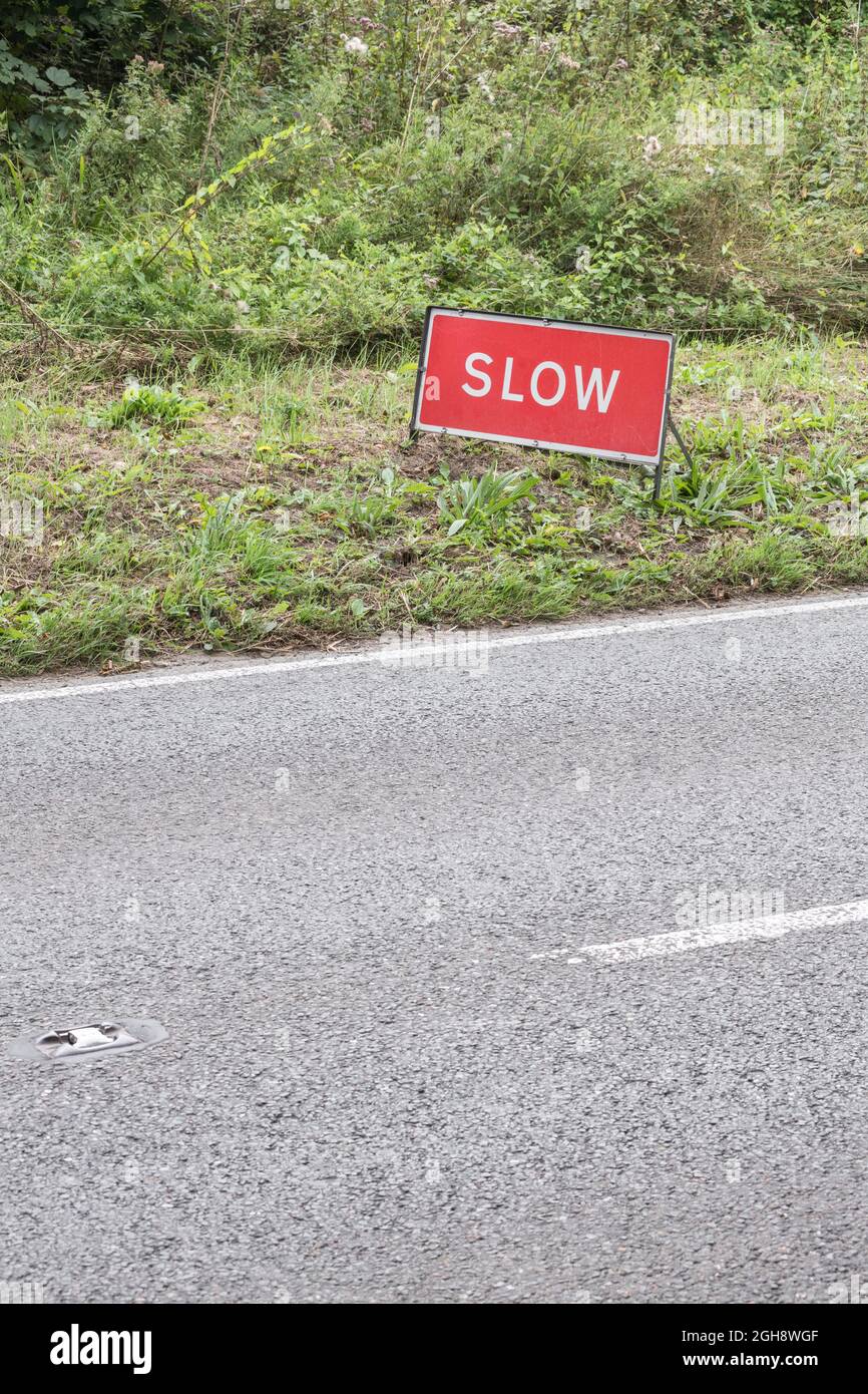 Red SLOW road sign on rural grass verge, warning of roadworks ...
