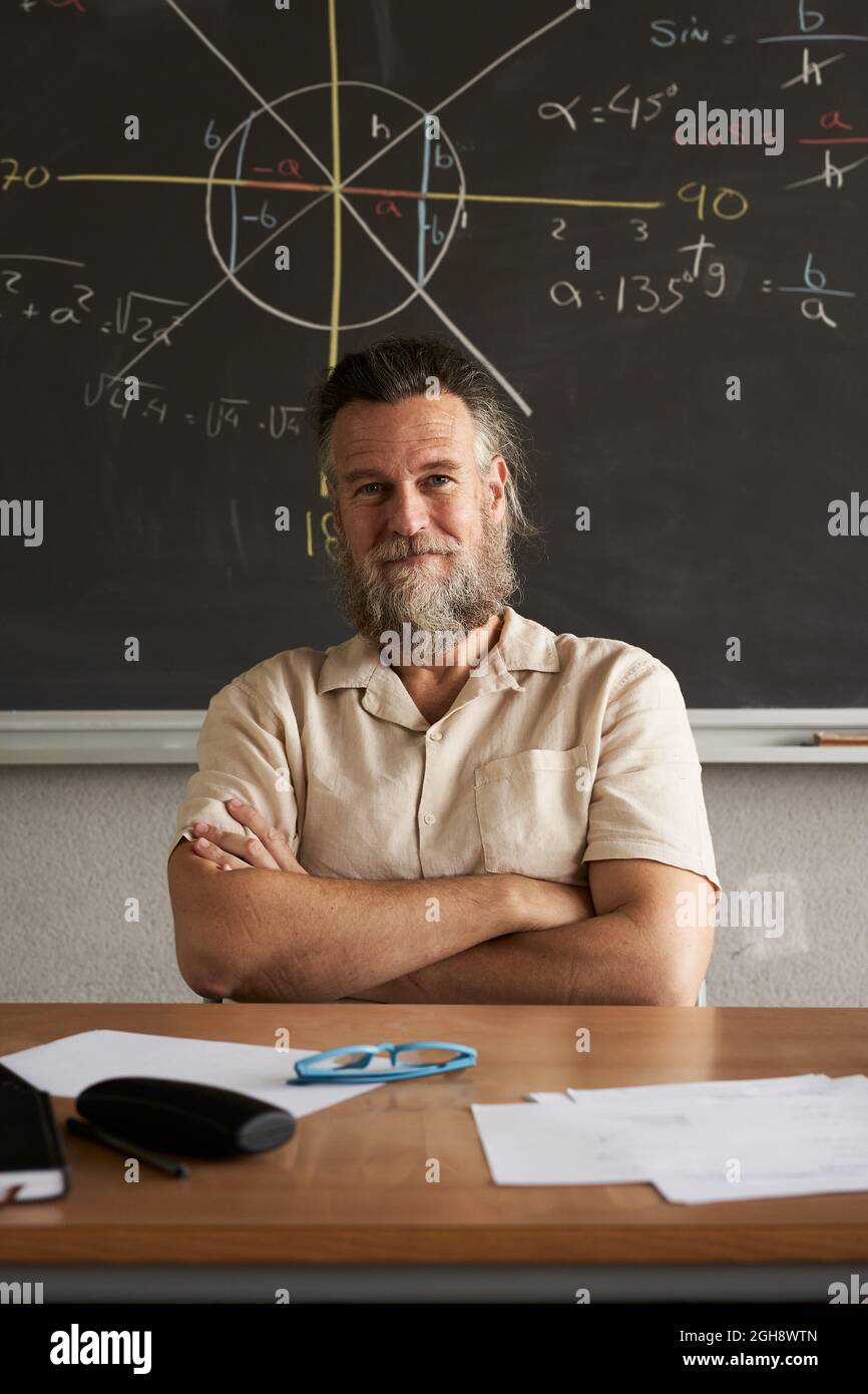 Vertical photo. Cheerful teacher looks at the camera with his arms ...