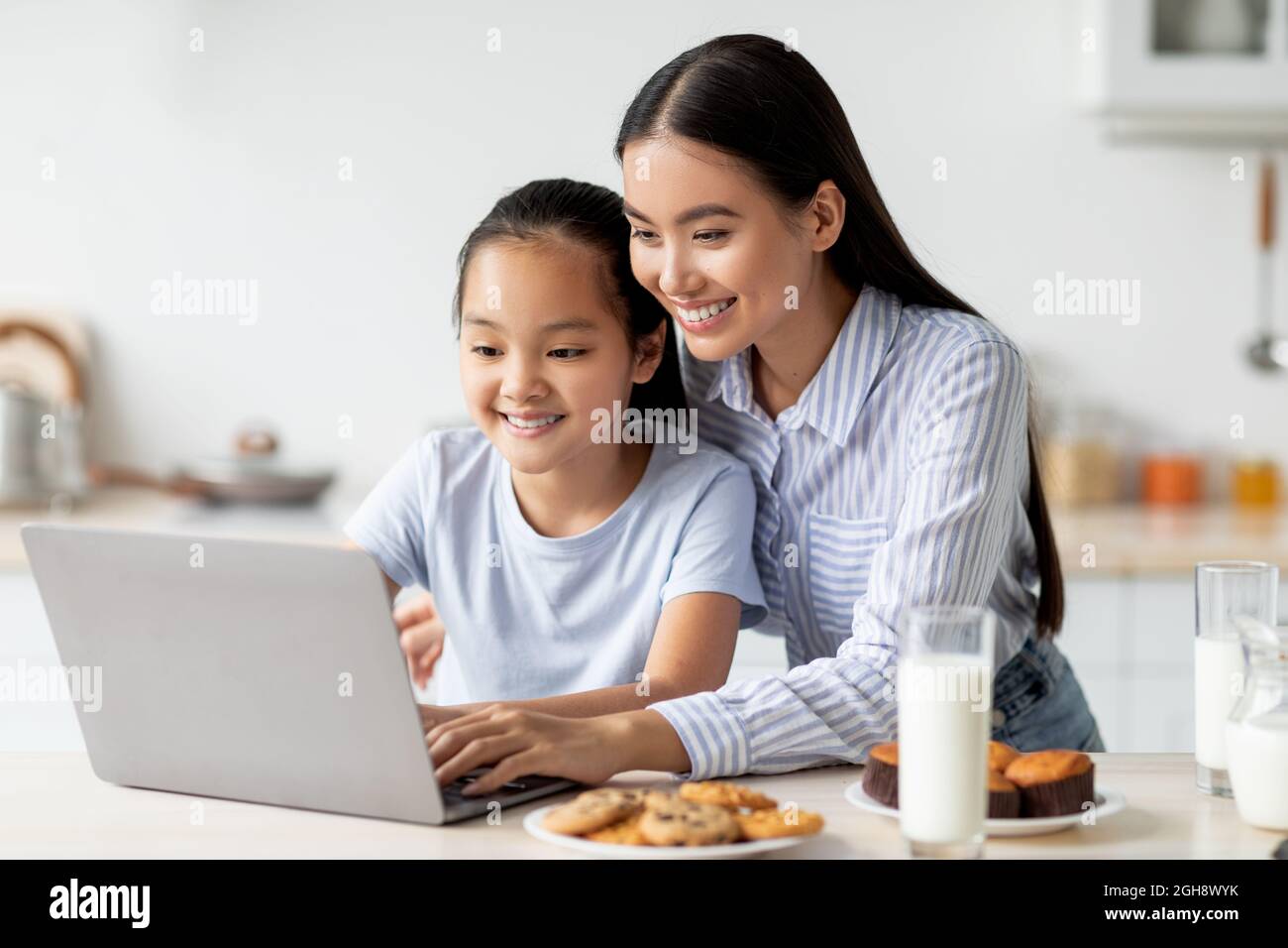 Happy asian mother and kid using laptop together, sitting at kitchen ...