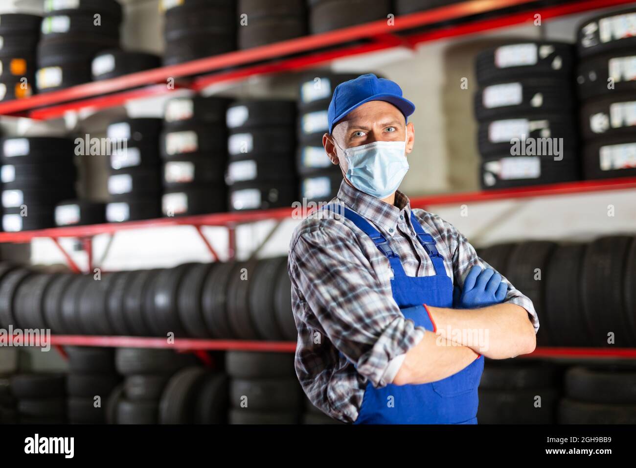 Portrait of professional male mechanician in face mask posing at auto ...