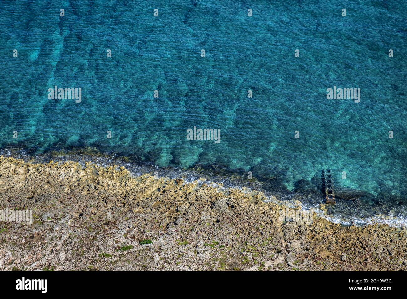 Overhead shot of the coastal line with clear blue water and brown sand ...