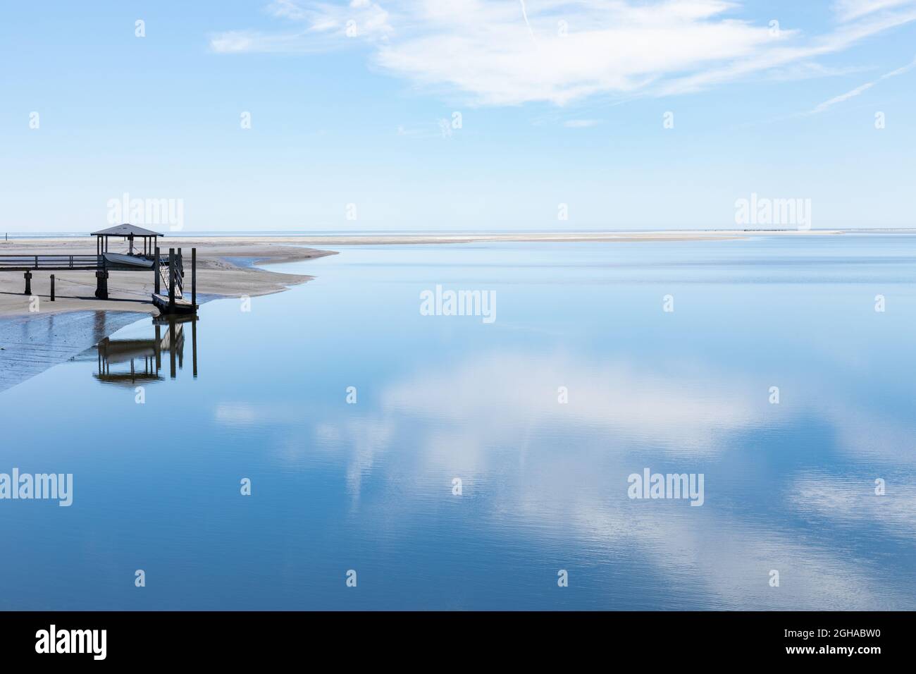 Floating boat dock at low tide, blue sky reflected in still water of ...
