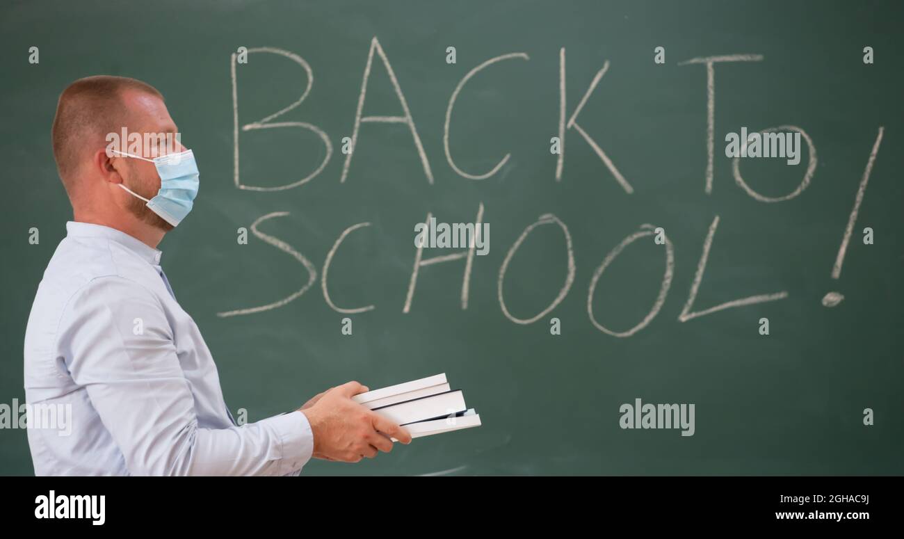 Teacher with face mask welcoming children back at school after lockdown ...