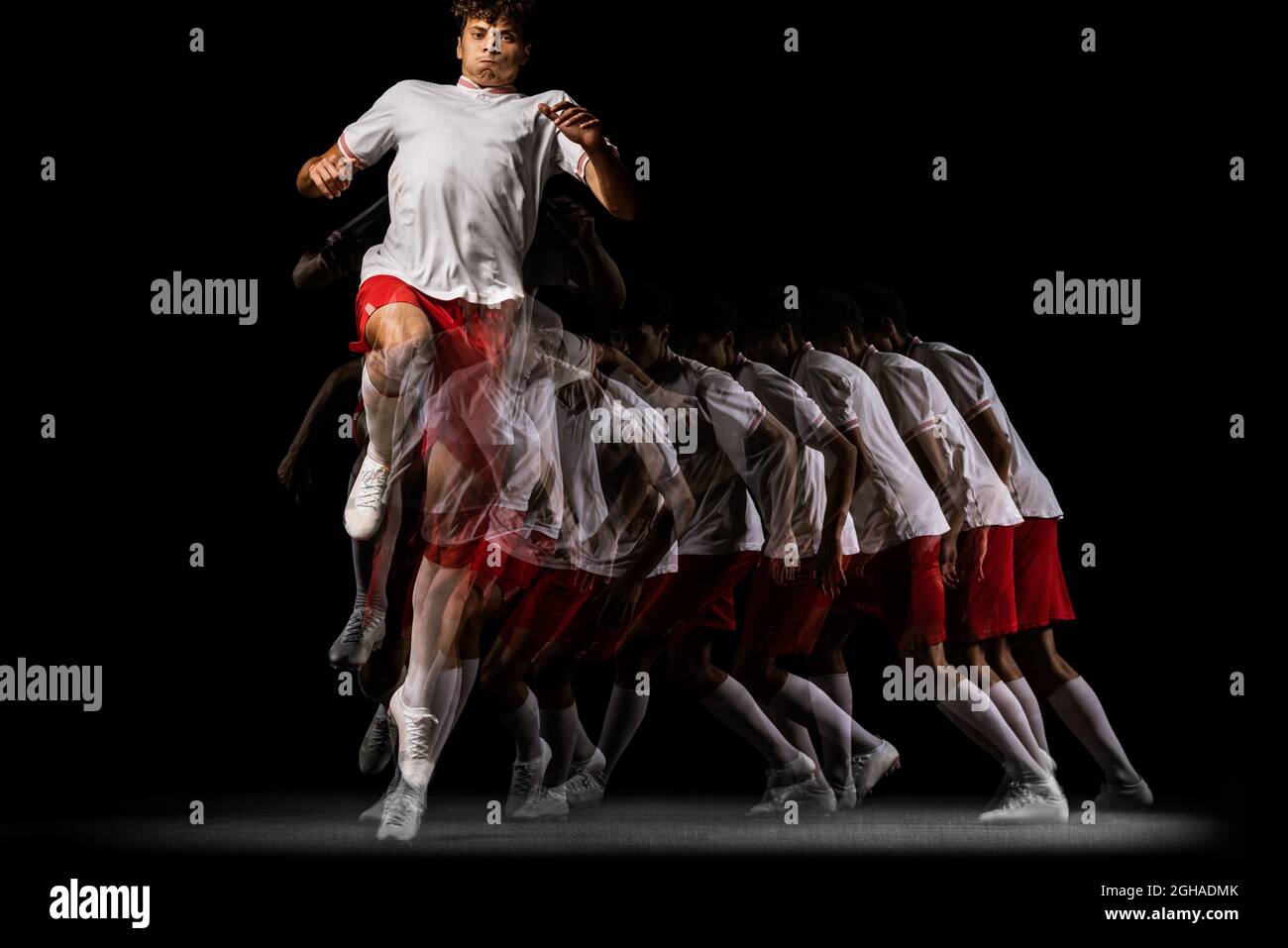 Young professional sportsman playing football alone isolated on black ...