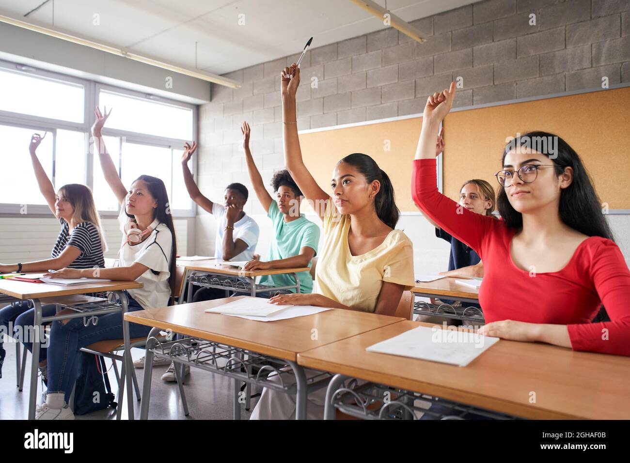 Multi-ethnic students in class with hands raised. Concentrated young ...