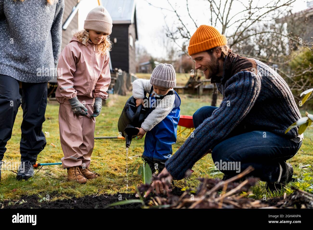 Man guiding son using watering can by girl while doing gardening at ...