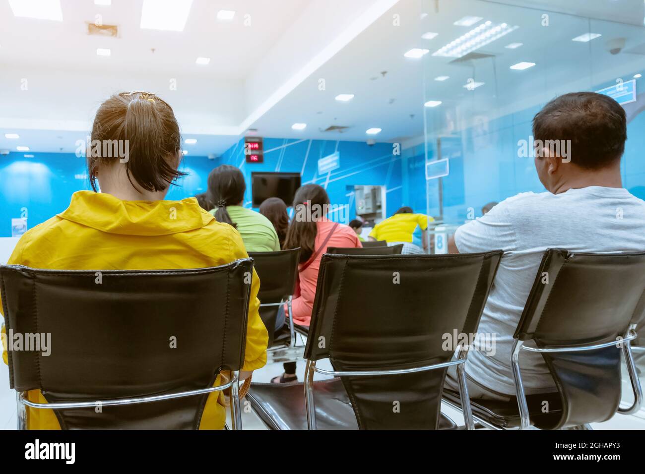 Back view of female customers sitting and wait in queues to financial ...