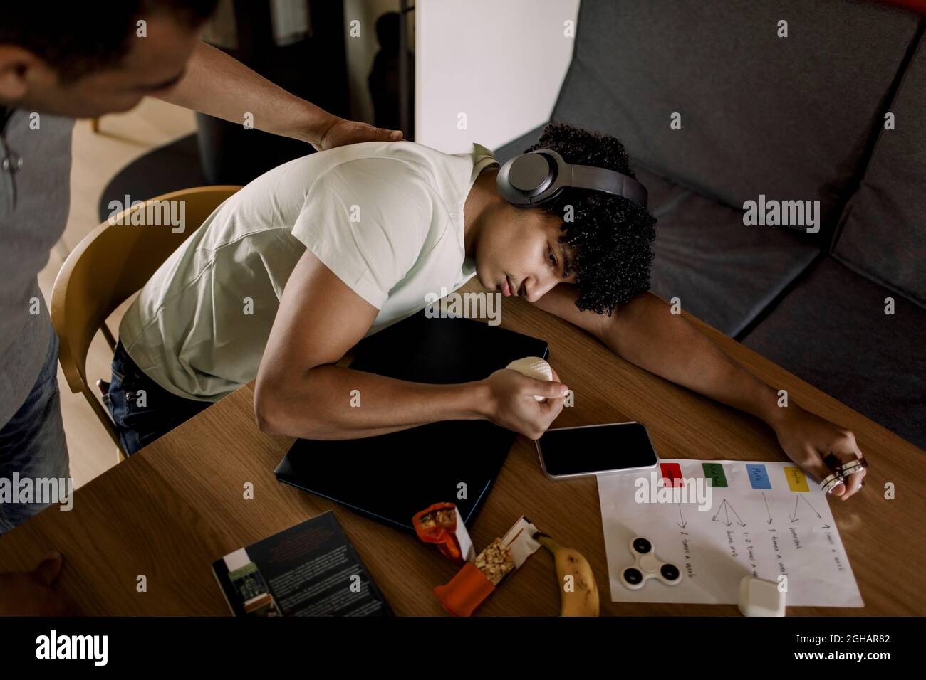 High angle of father looking at exhausted son resting over table at ...