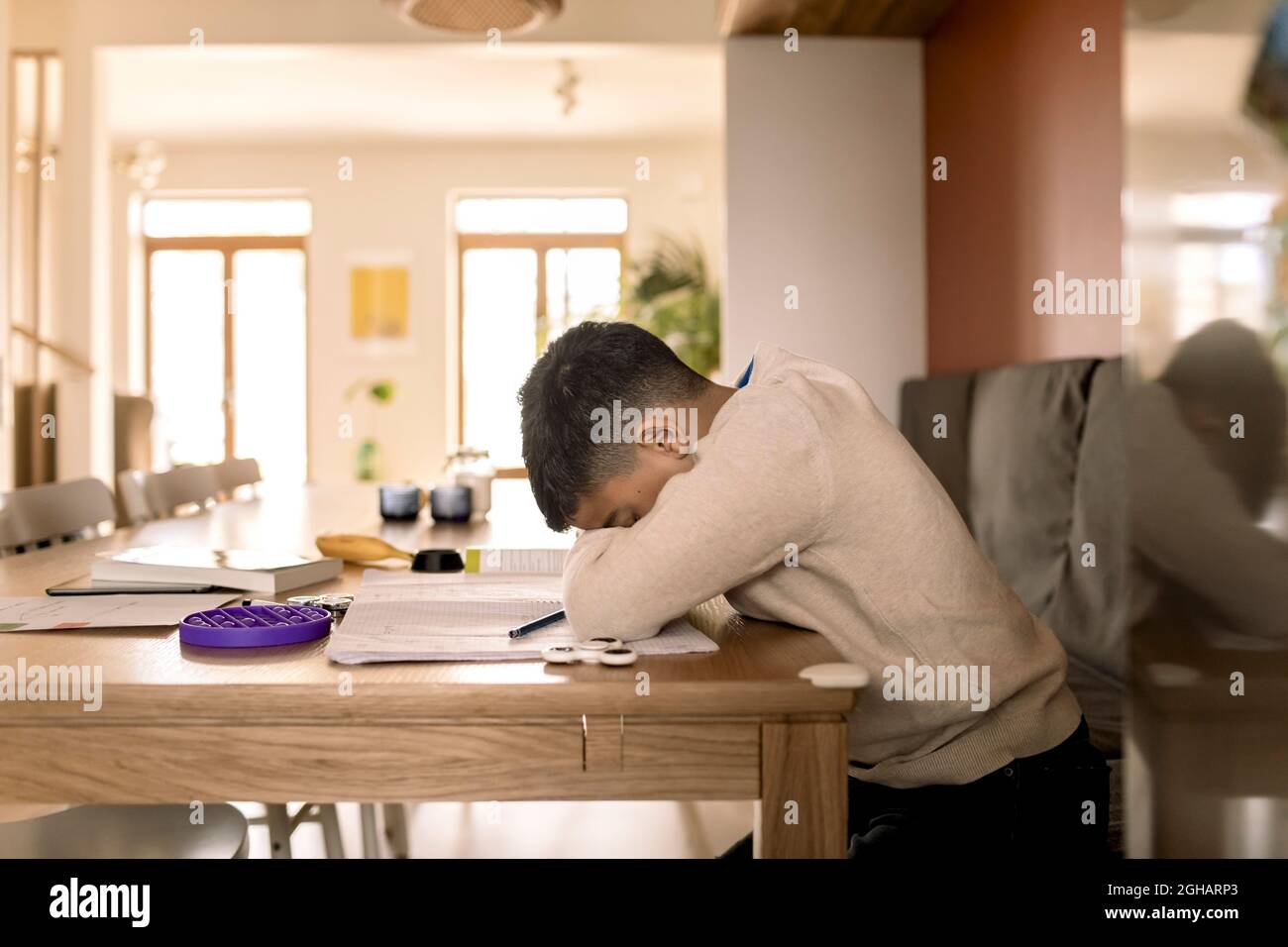 Tired boy with head down over table in living room Stock Photo - Alamy