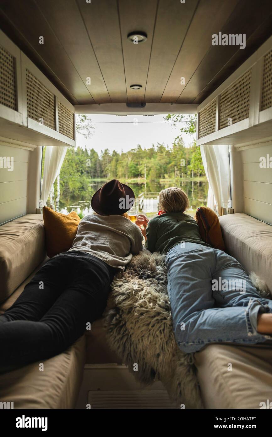 Rear view of couple looking at view while lying down in camping van ...