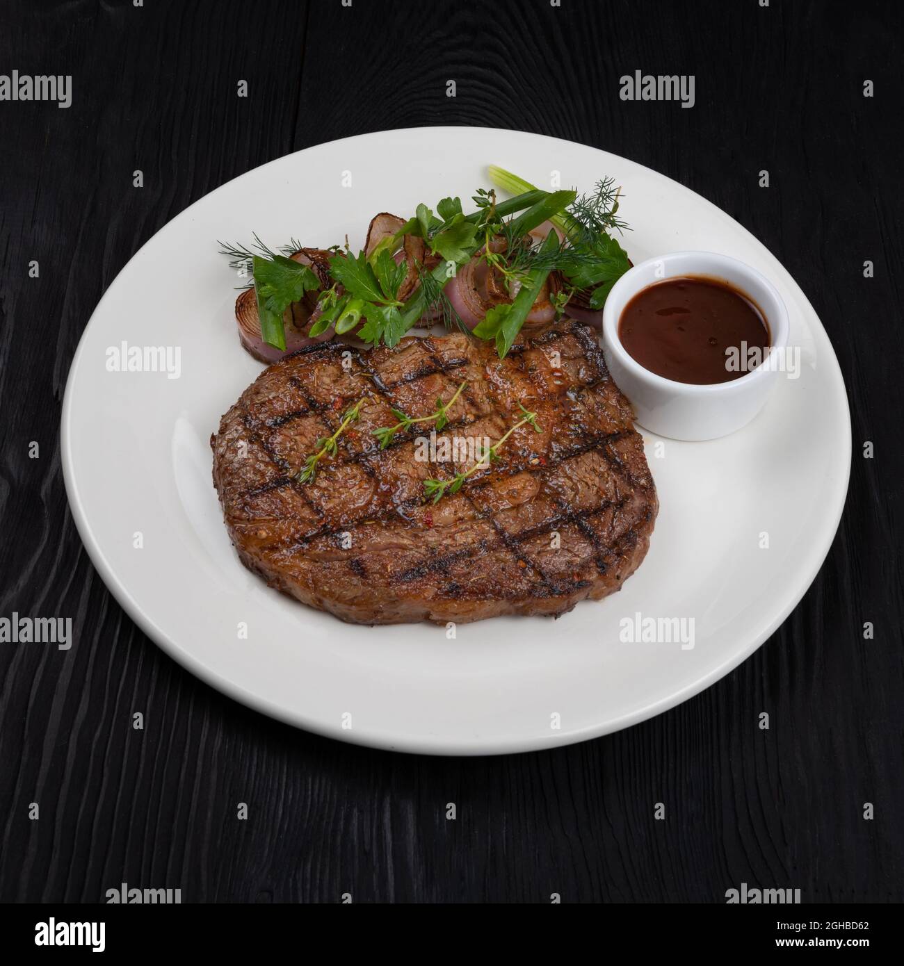 Grilled black angus steak ribeye on white plate on black wooden ...