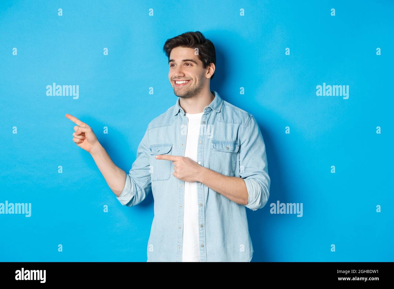 Handsome adult man introduce product, looking and pointing fingers left ...