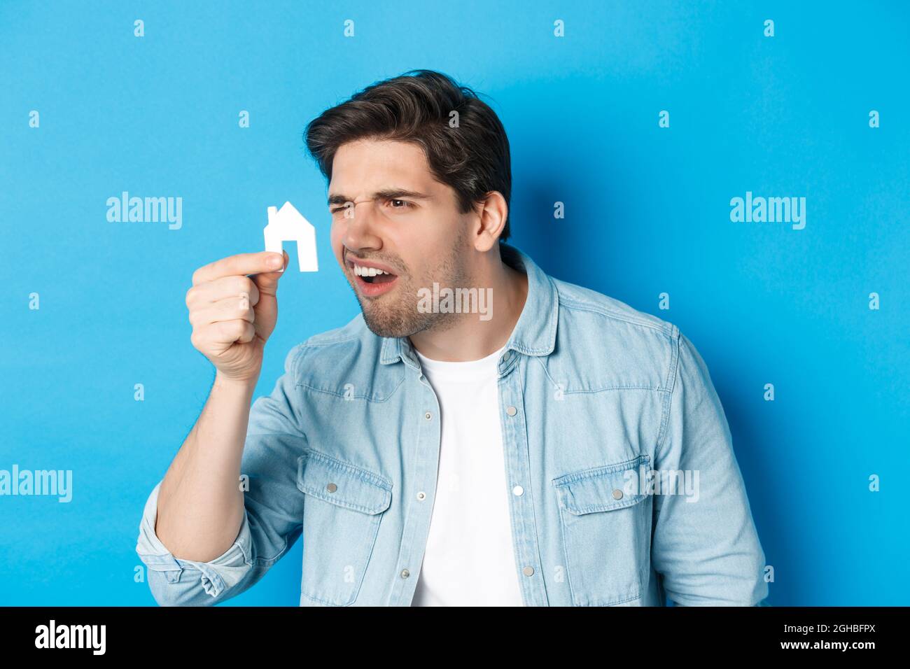 Real estate concept. Man looking at tiny house maket with confused face ...