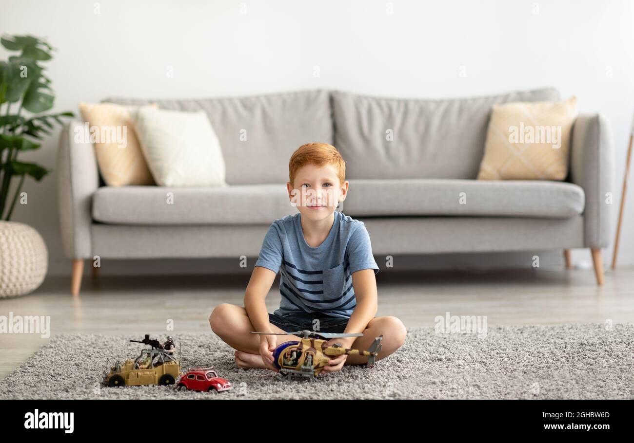 Cheerful boy sitting on carpet, playing with helicopter and cars Stock ...