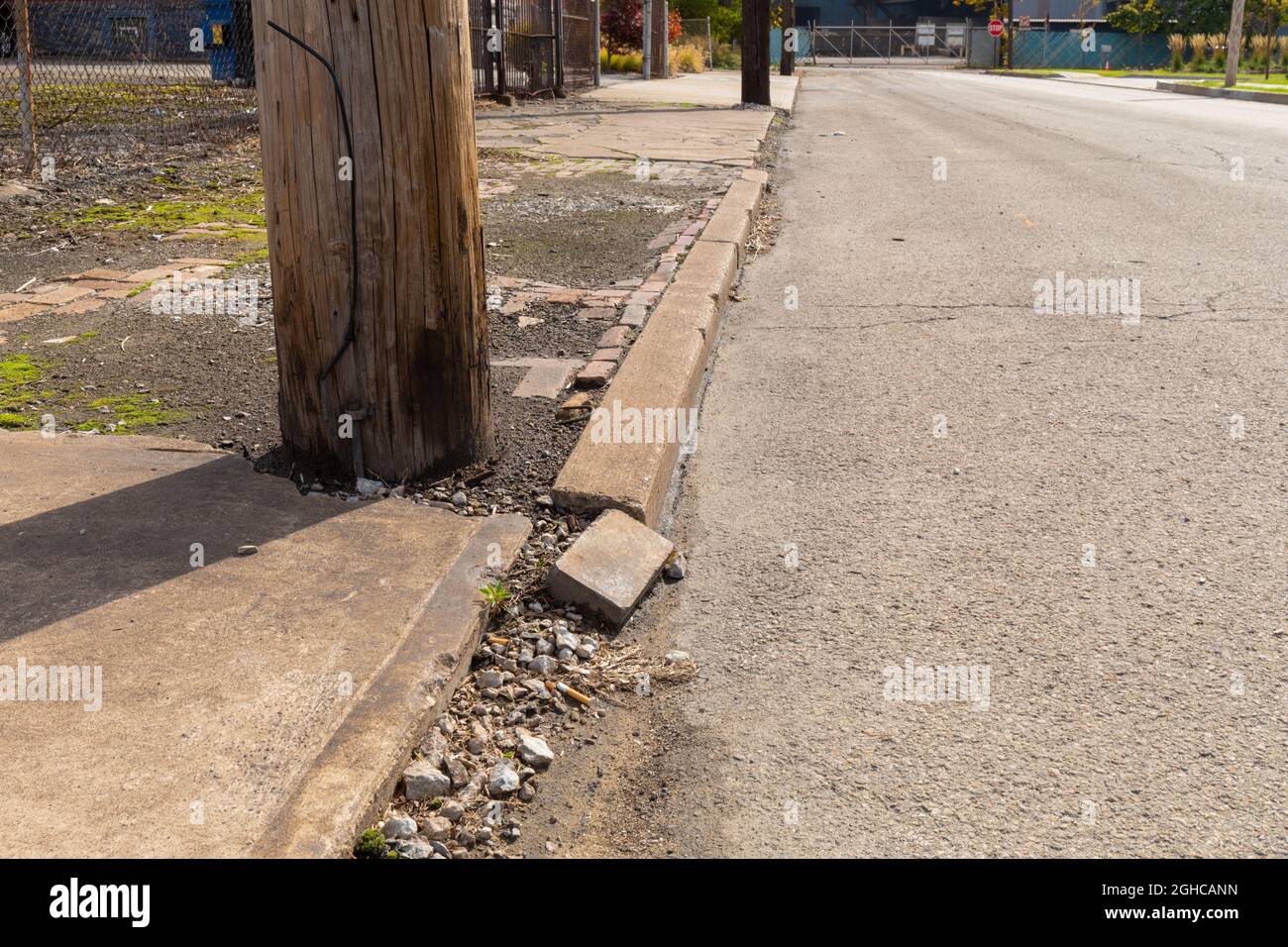 Wood utility pole surrounded by crumbling sidewalk and asphalt street ...