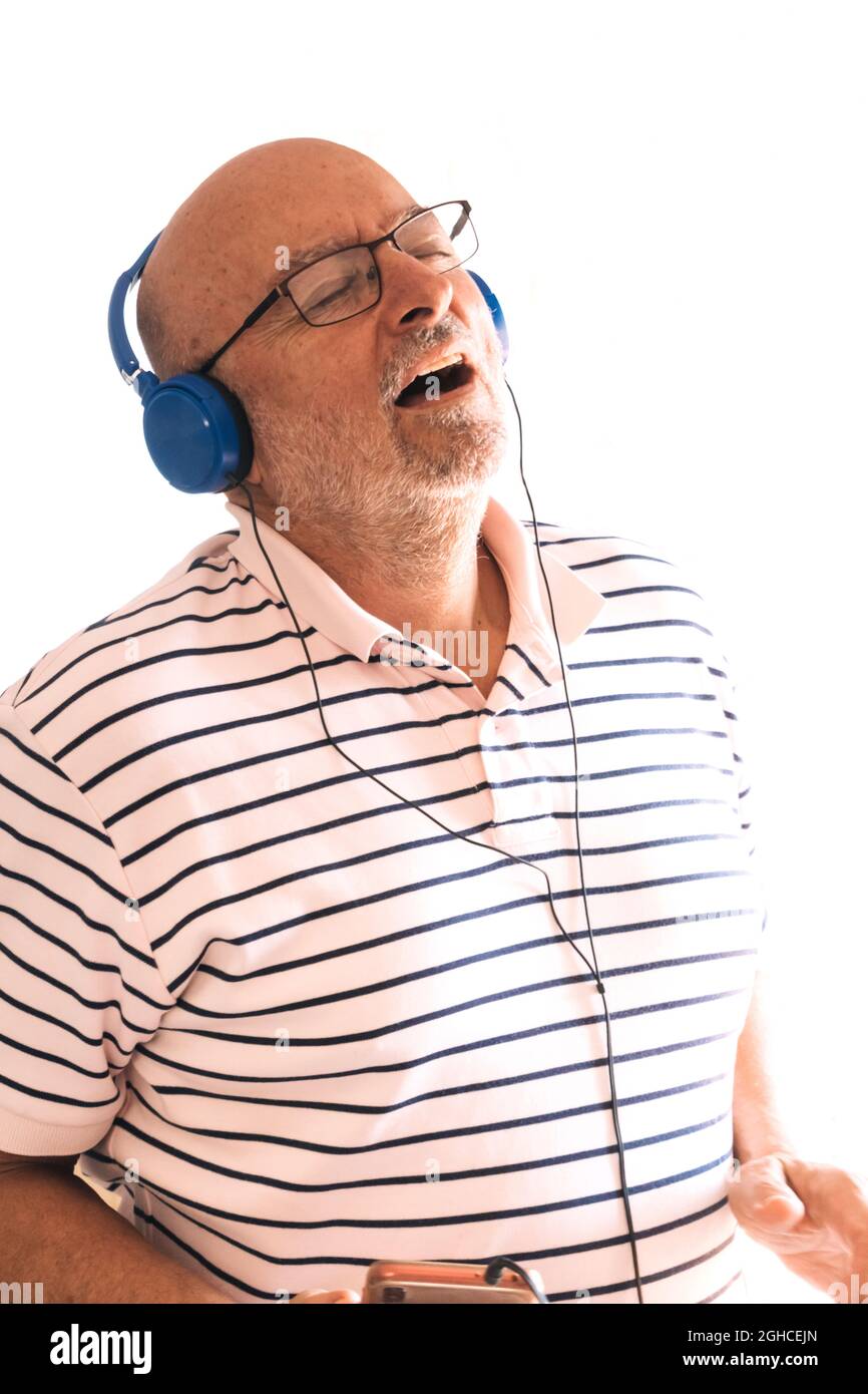 Happy old man in headphones singing with wall background, isolated with ...