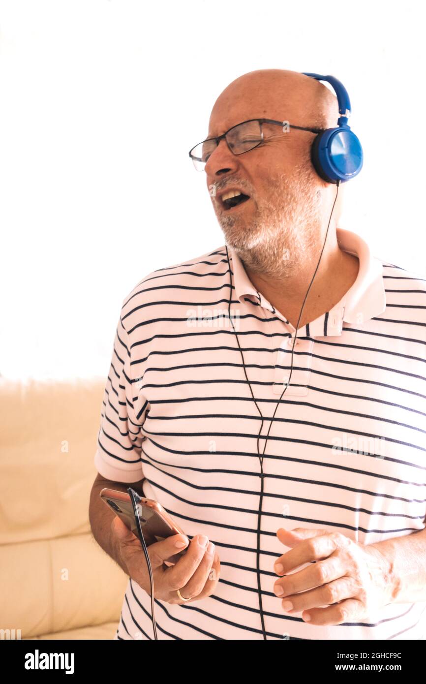 Happy old man in headphones singing with wall background, isolated with ...