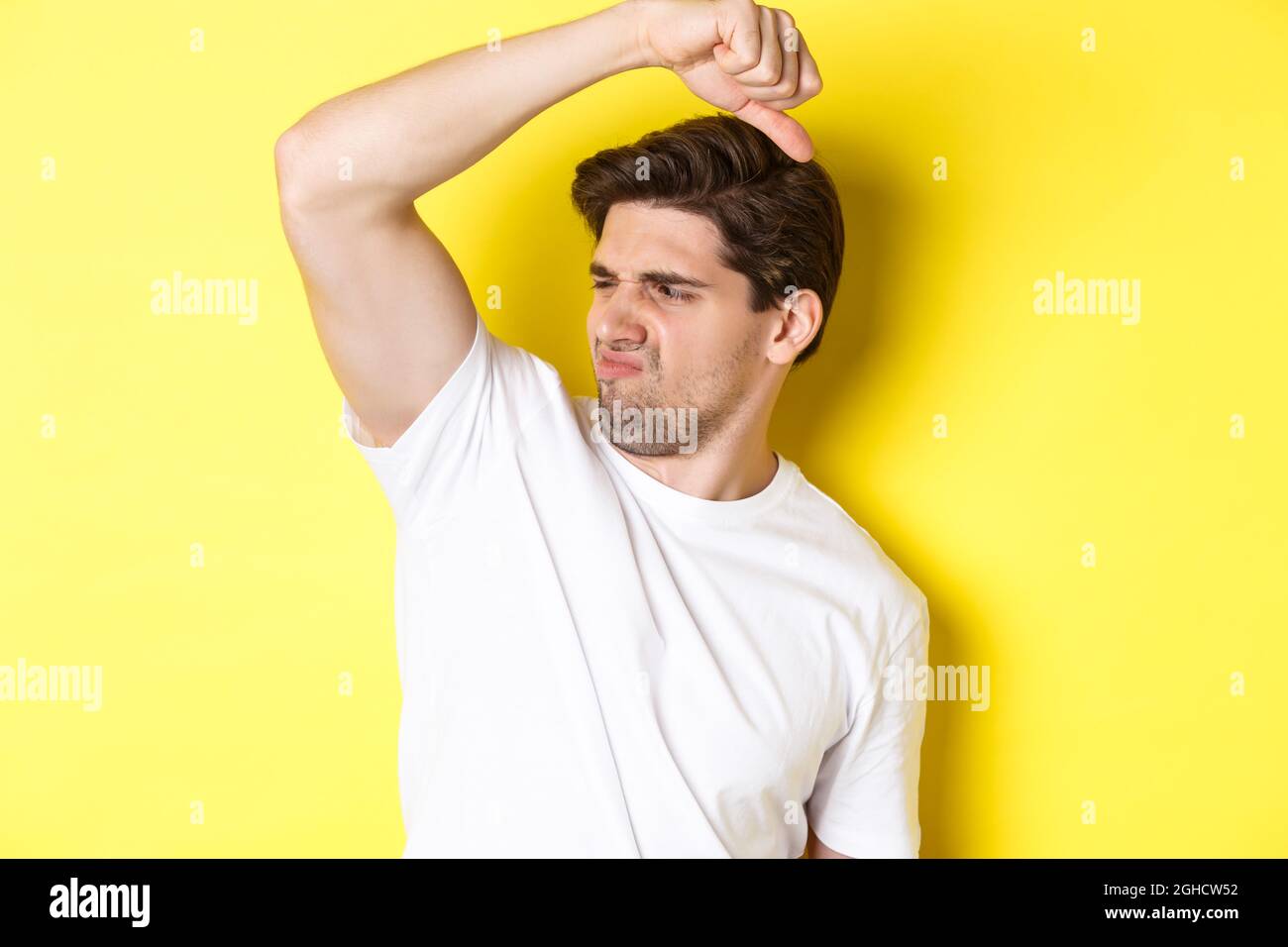 Man in sweat smelling his armpit, standing in white t-shirt and ...