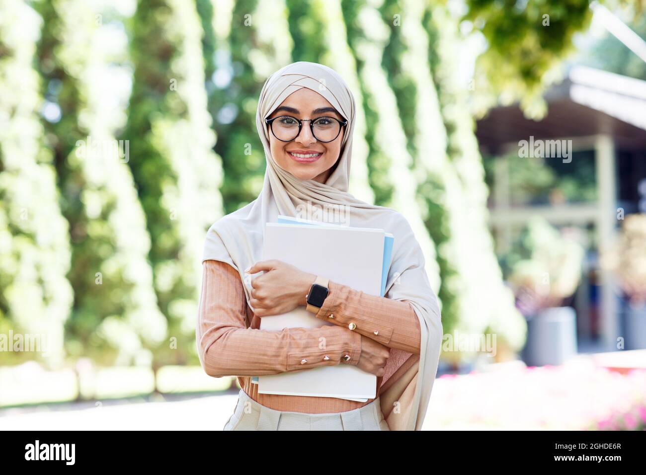Cheerful cute young middle eastern lady in hijab, glasses holds books ...