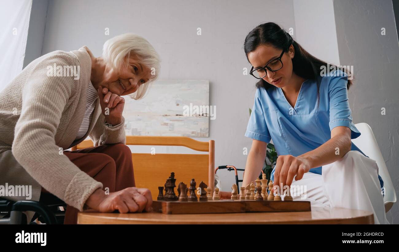 happy elderly woman and nurse playing chess in nursing home Stock Photo ...