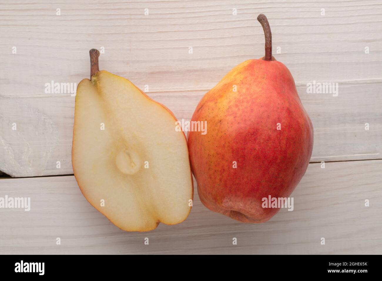 One whole and one half sweet, red pears on a white wooden table, close ...