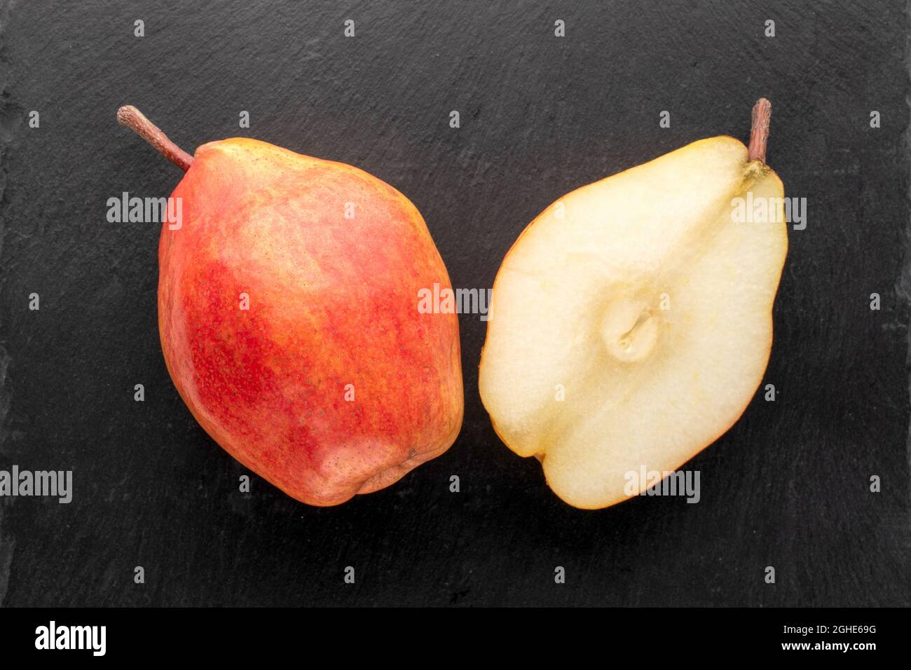 One whole and half of ripe red pears, close-up, on a slate board, top ...